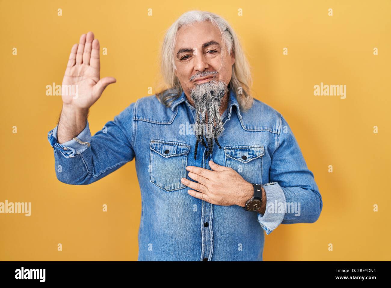 Middle age man with grey hair standing over yellow background swearing ...