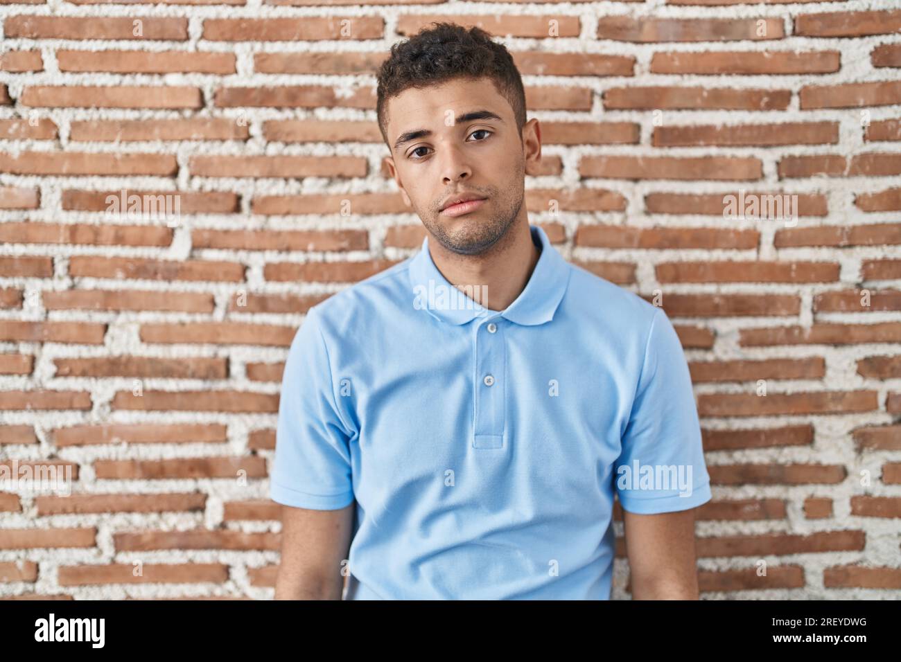 Brazilian young man standing over brick wall looking sleepy and tired ...