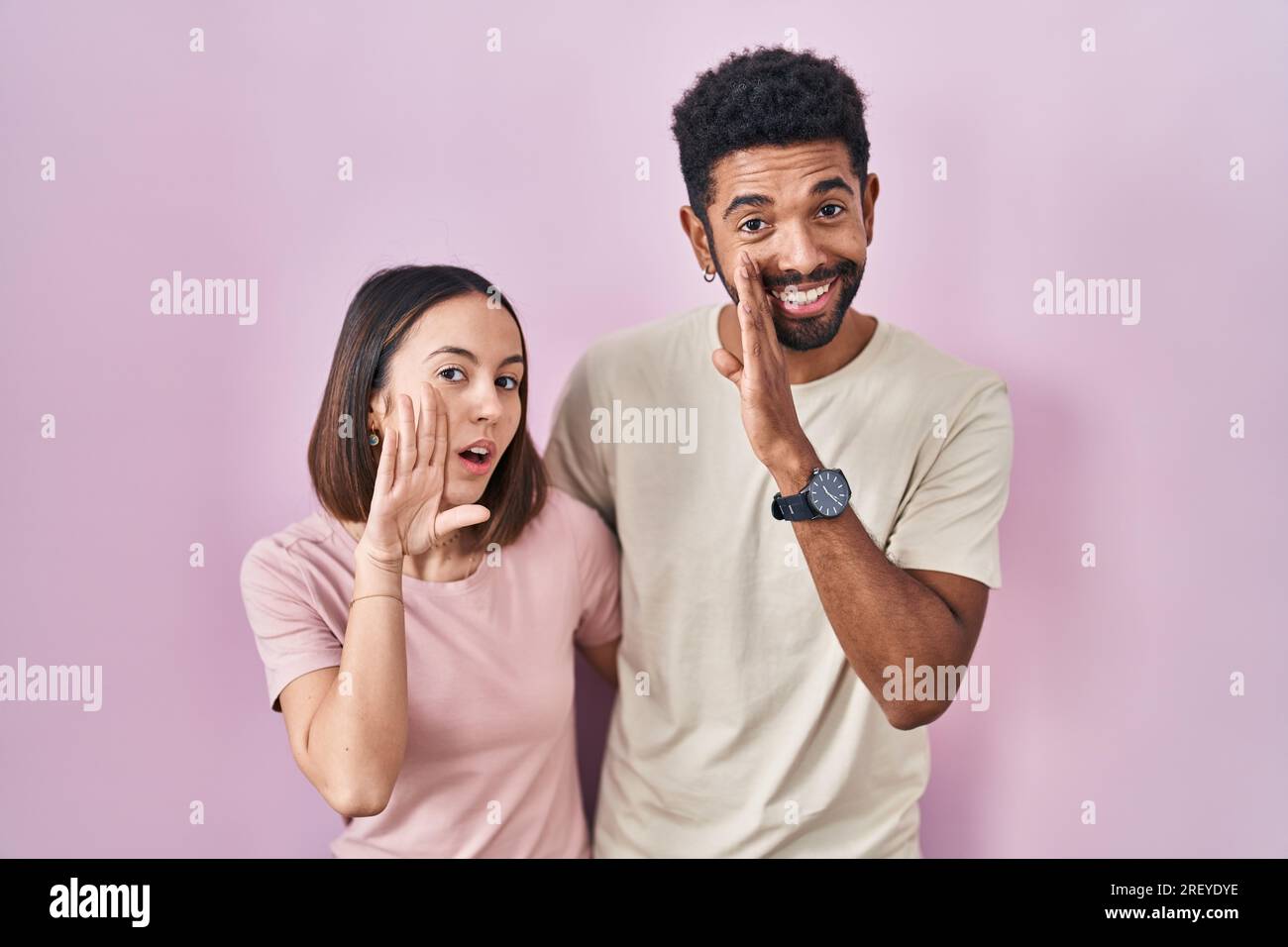 Young hispanic couple together over pink background hand on mouth ...