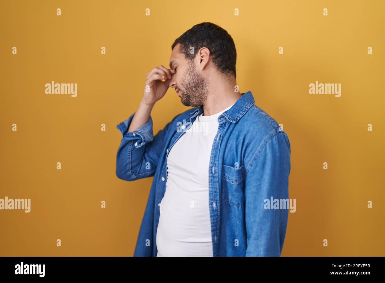 Hispanic man standing over yellow background tired rubbing nose and ...