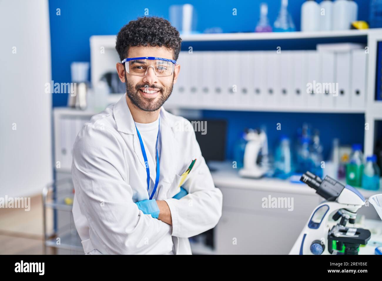 Young arab man wearing scientist uniform sitting with arms crossed ...