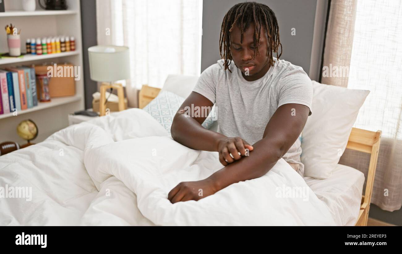 African american man scratching arm for itchy sitting on bed at bedroom ...