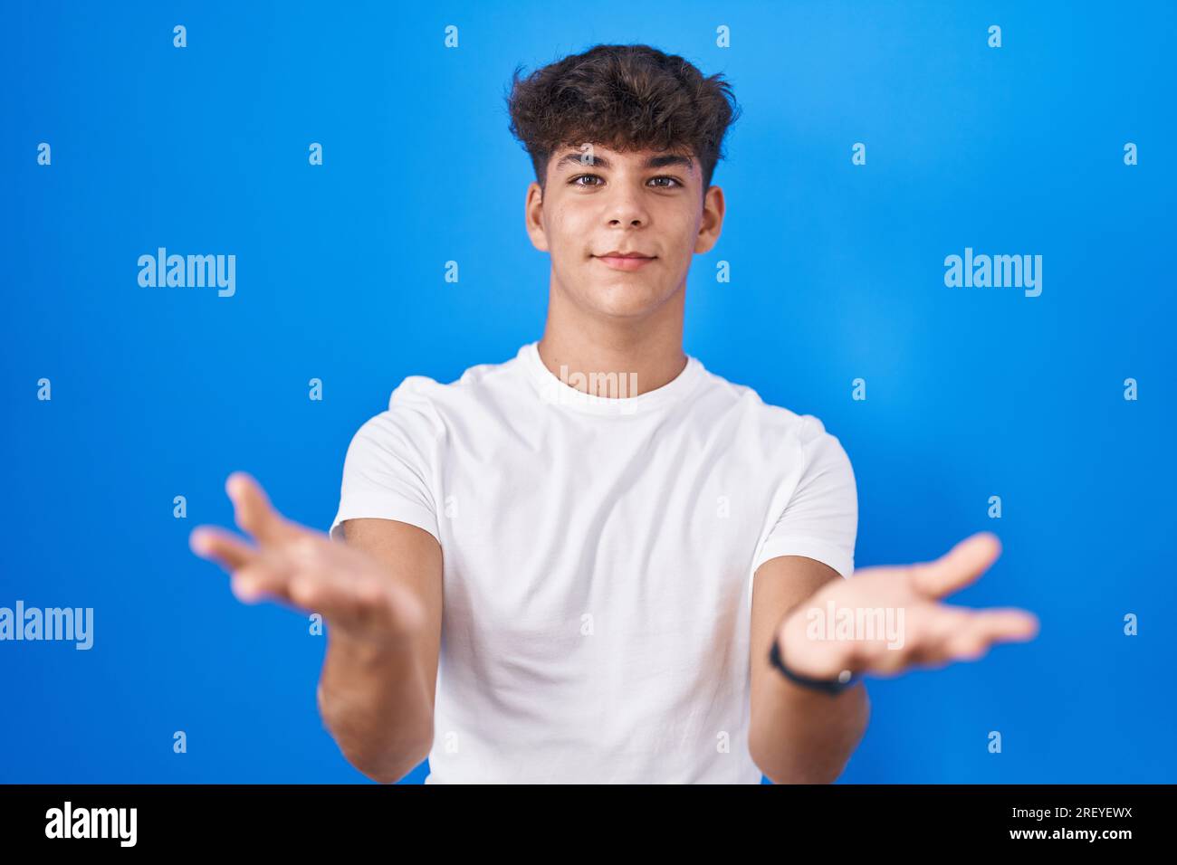 Hispanic teenager standing over blue background smiling cheerful ...
