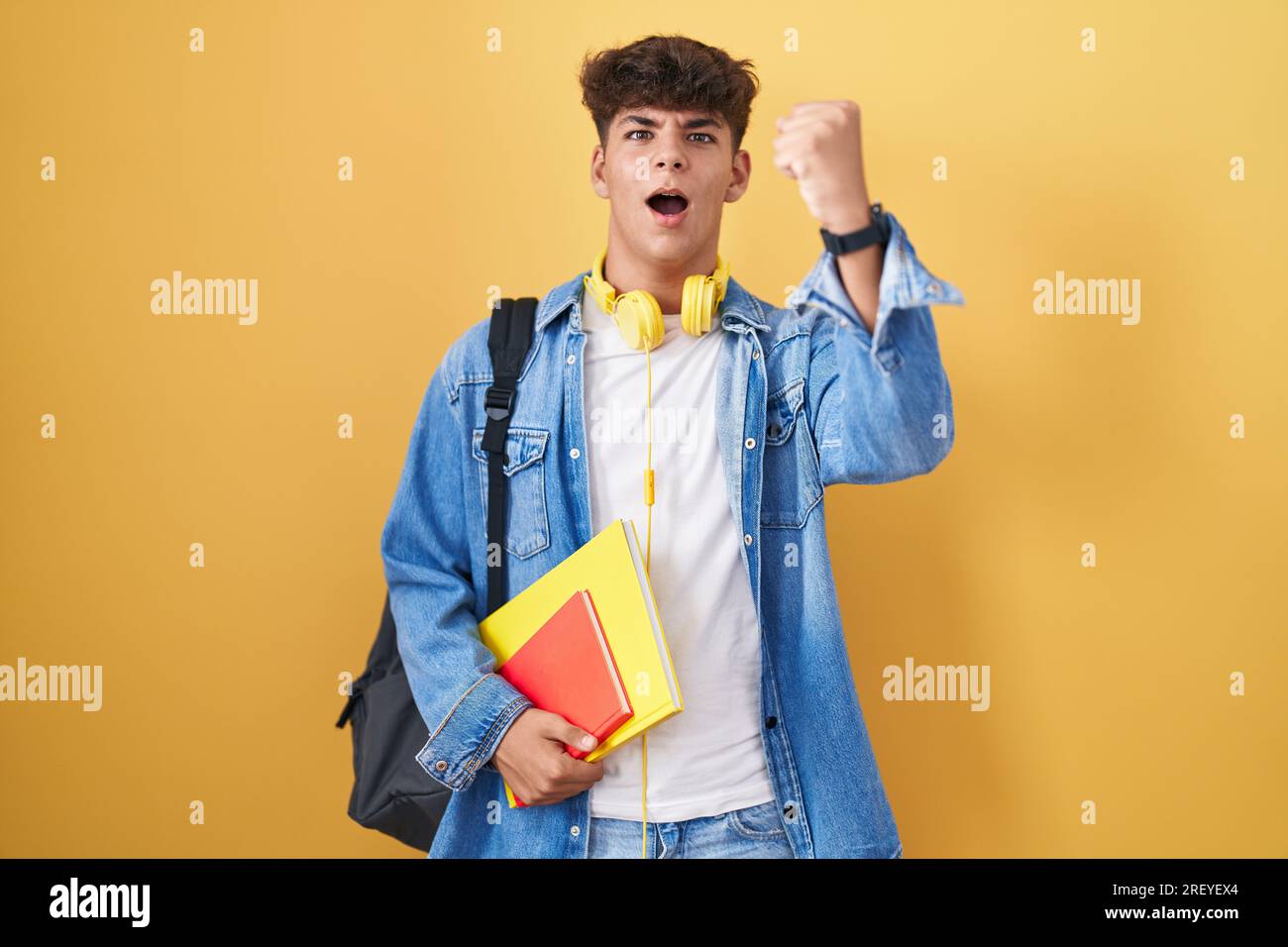 Hispanic teenager wearing student backpack and holding books angry and ...