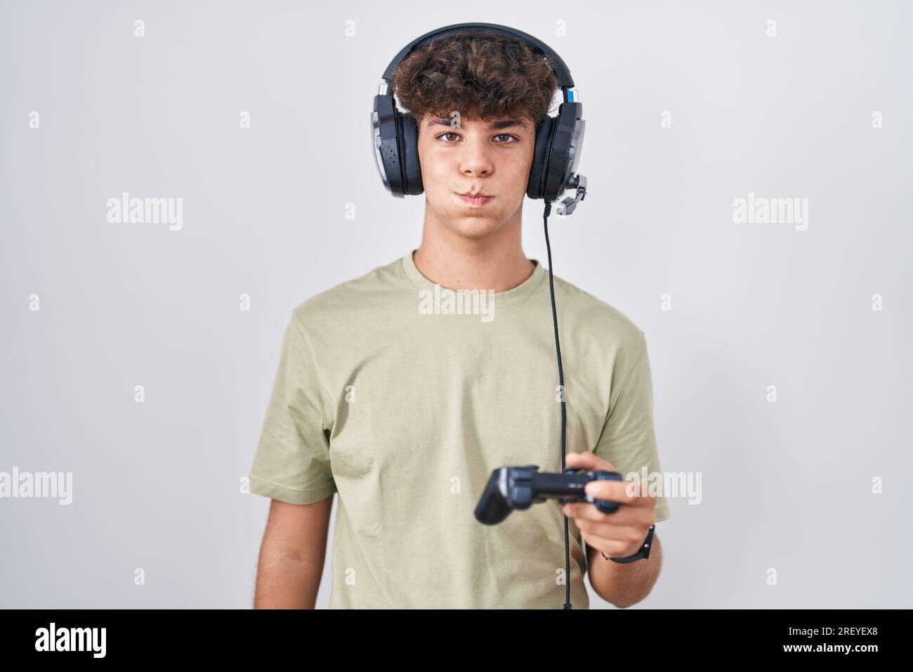 Hispanic teenager playing video game holding controller puffing cheeks ...