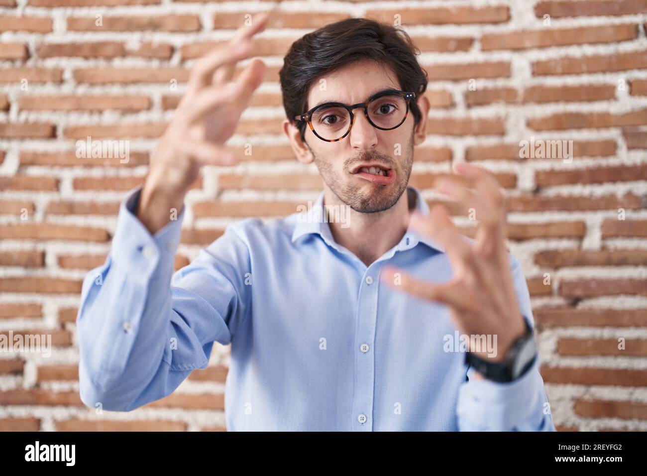 Young hispanic man standing over brick wall background shouting ...