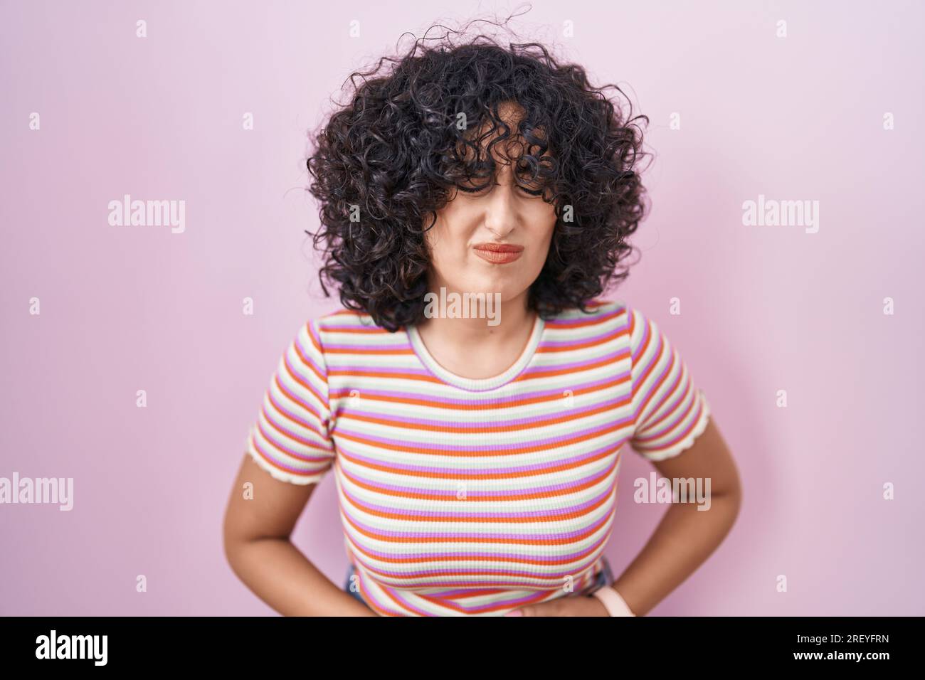 Young middle east woman standing over pink background with hand on ...