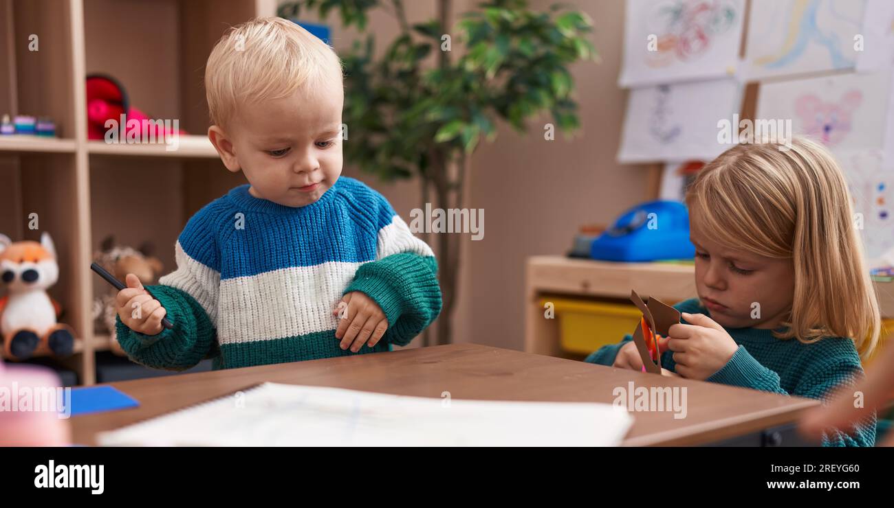 Adorable boy and girl student cutting paper sitting on table at ...