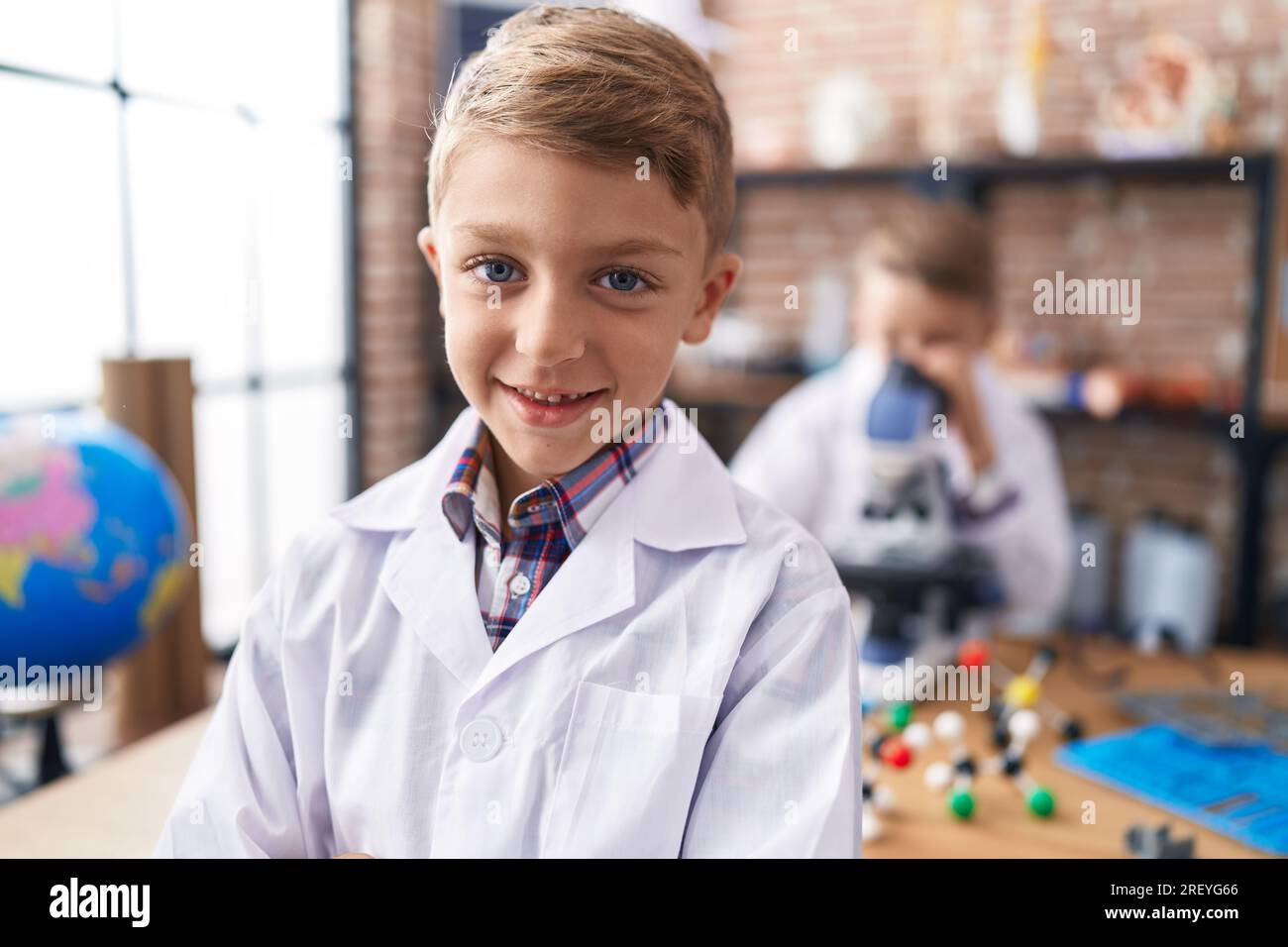 Adorable boys students using microscope standing with arms crossed ...
