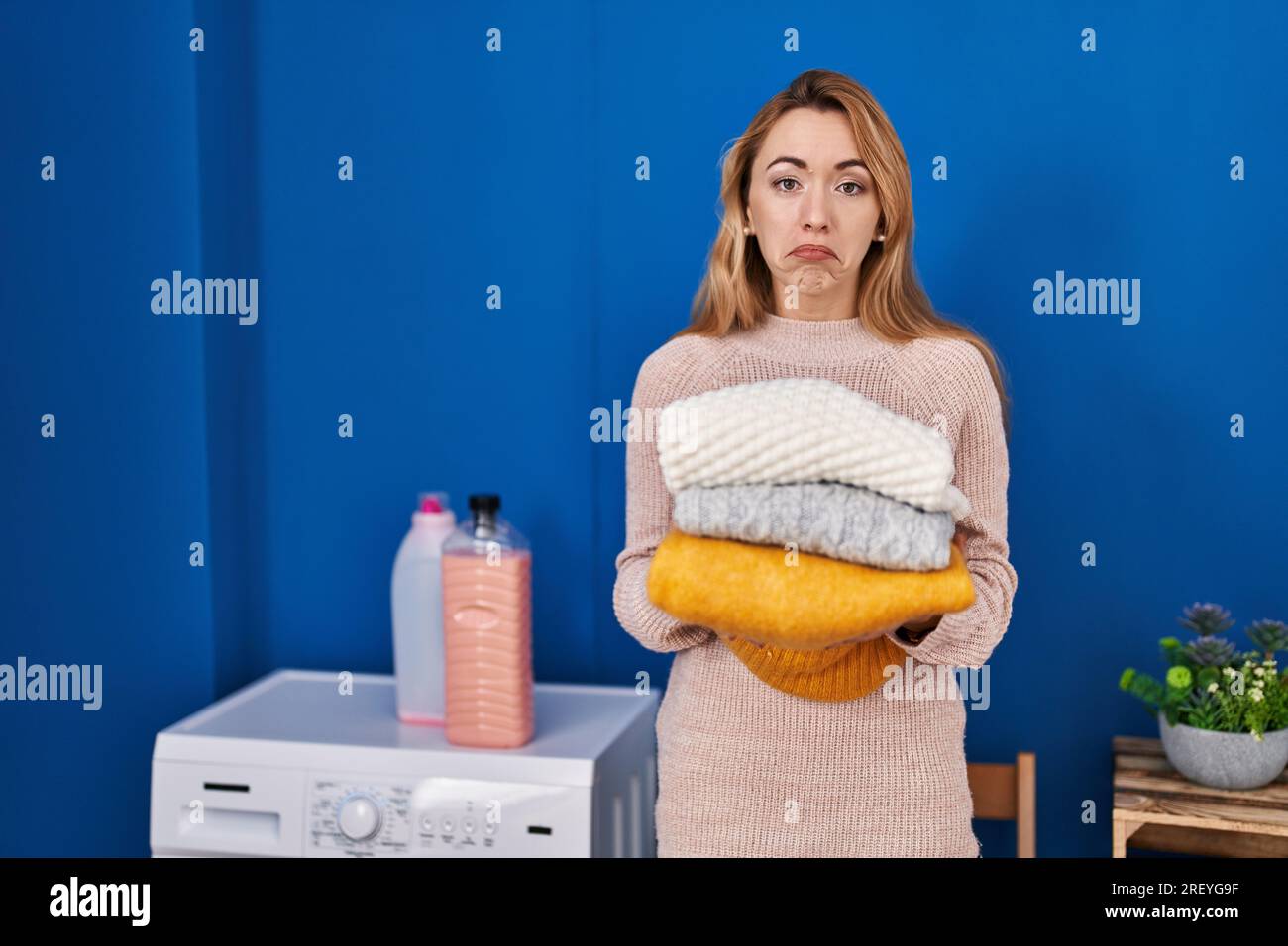 Hispanic woman holding folded laundry after laundry depressed and worry for distress, crying ...