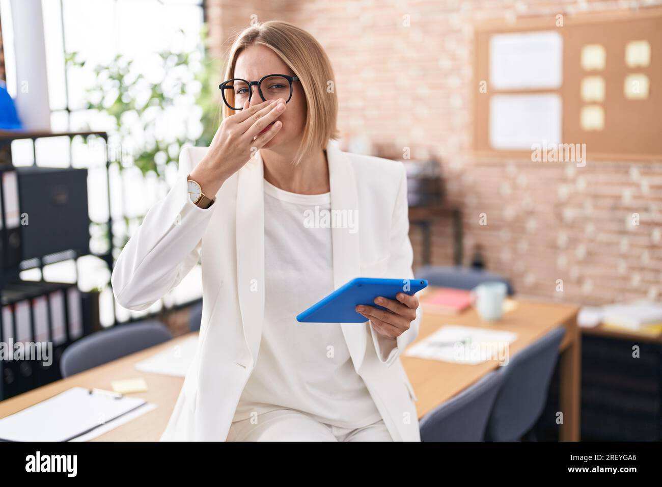 Young caucasian woman working at the office wearing glasses smelling ...