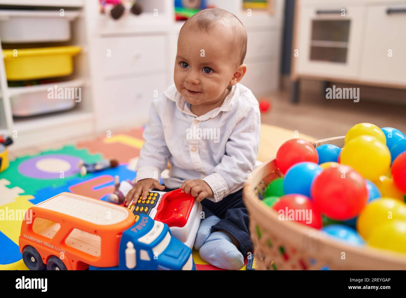 Adorable caucasian boy playing with balls sitting on floor at ...