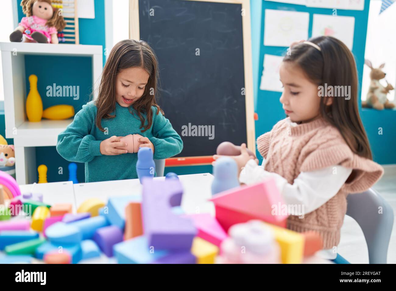 Adorable girls playing with construction blocks sitting on table at ...
