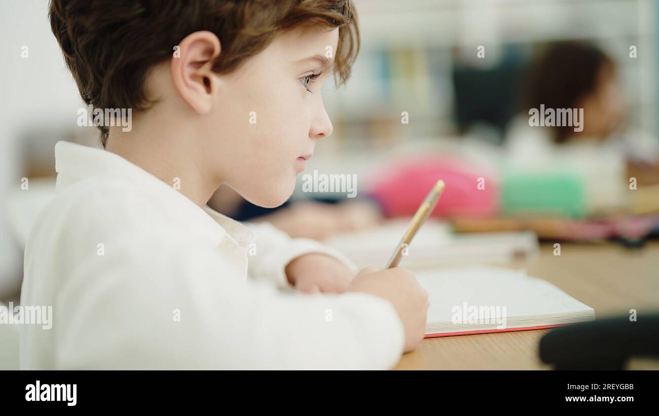 Adorable caucasian boy student writing on notebook studying at ...