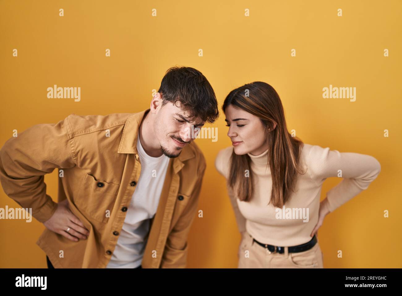 Young hispanic couple standing over yellow background suffering of ...