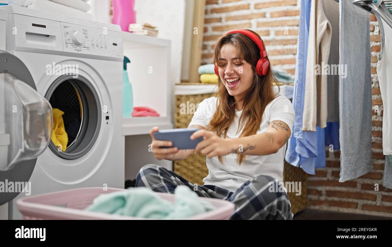 Young beautiful hispanic woman playing video game washing clothes at ...