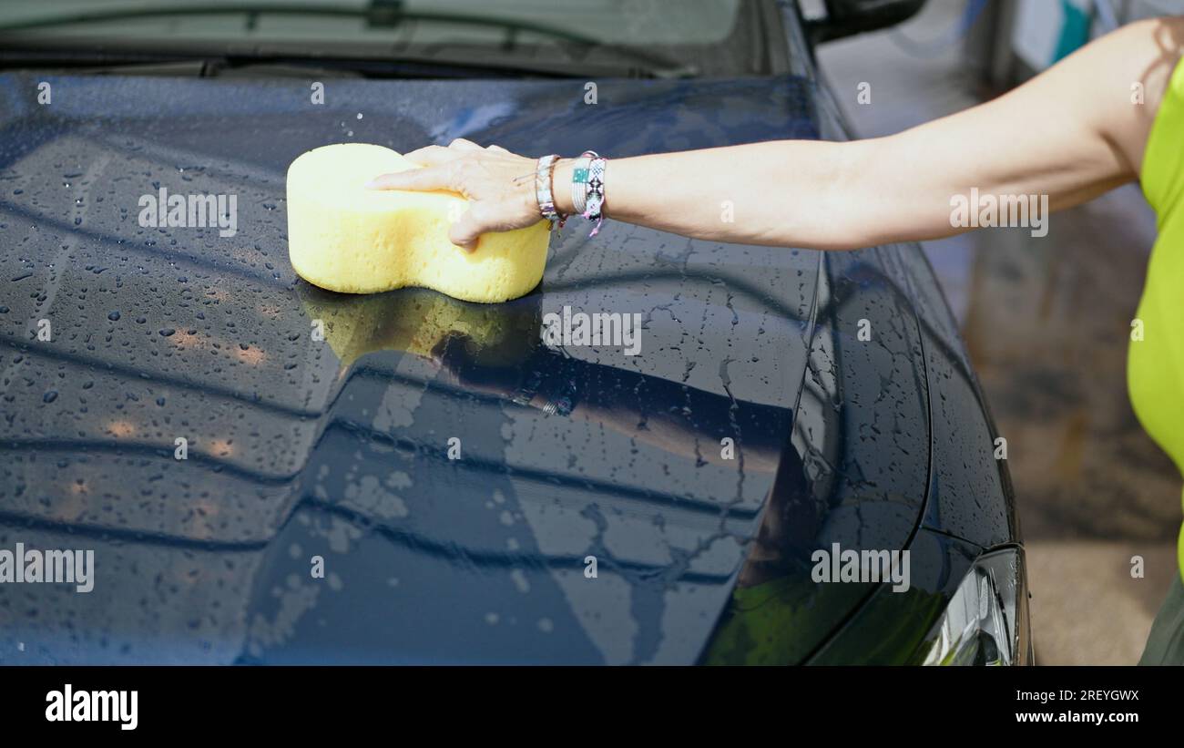 Middle age hispanic woman cleaning car with sponge at car wash station ...