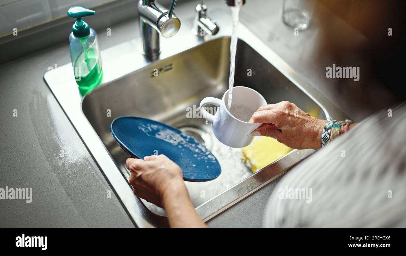 Middle age hispanic woman washing plates at the kitchen Stock Photo - Alamy