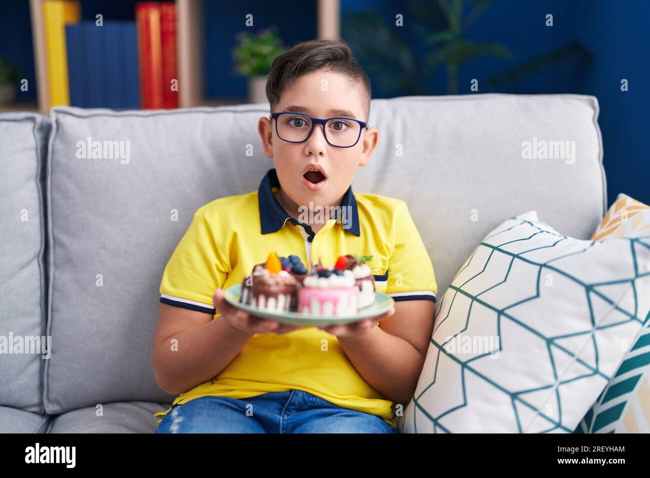 Young hispanic kid holding cake sweets in shock face, looking skeptical ...