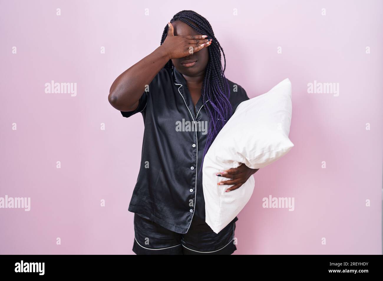 Young african woman wearing pijama hugging pillow covering eyes with ...