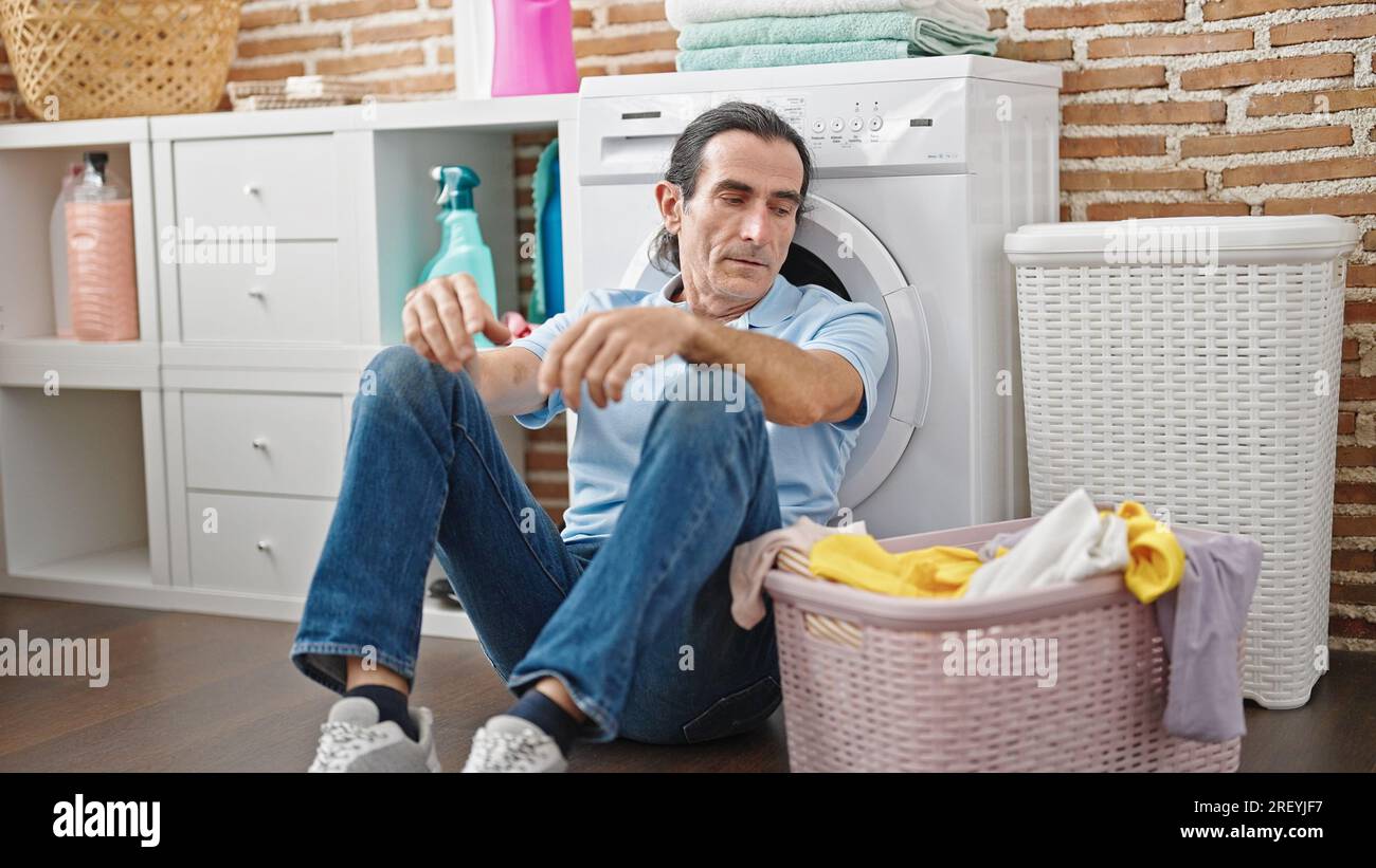 Middle age man leaning on washing machine with stressed at laundry room ...