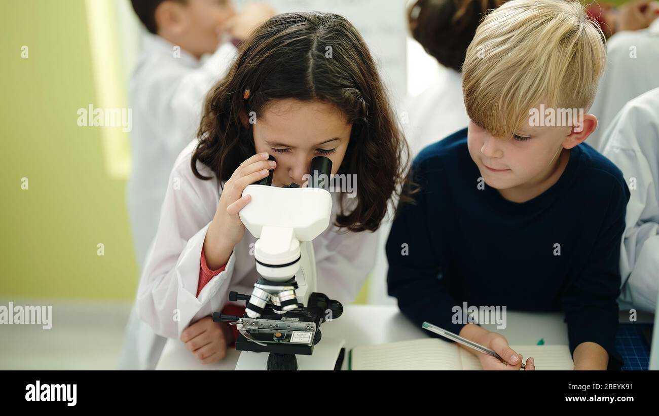 Adorable boy and girl students using microscope writing notes at ...