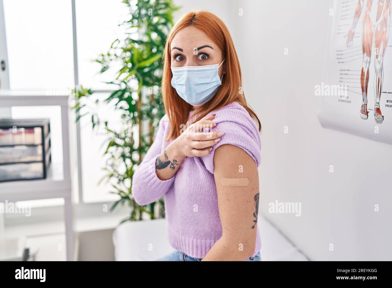 Young woman getting vaccine showing arm with band aid scared and amazed ...