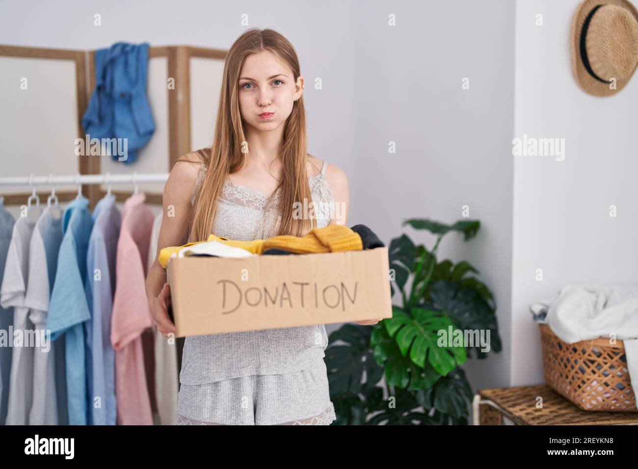 Young caucasian woman holding donations box for charity puffing cheeks ...