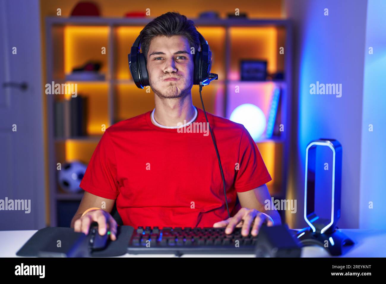 Young hispanic man playing video games puffing cheeks with funny face ...