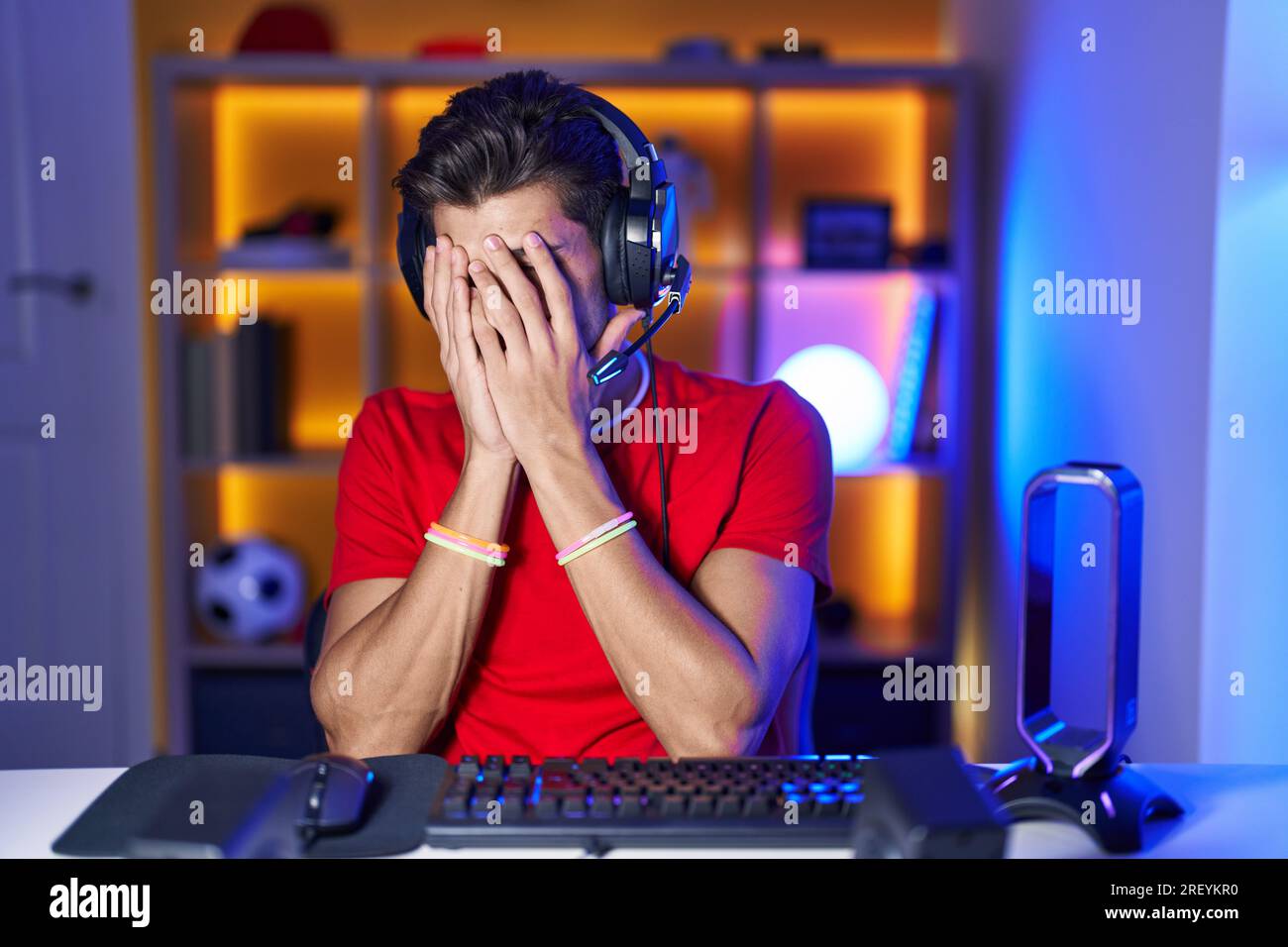 Young hispanic man playing video games with sad expression covering ...