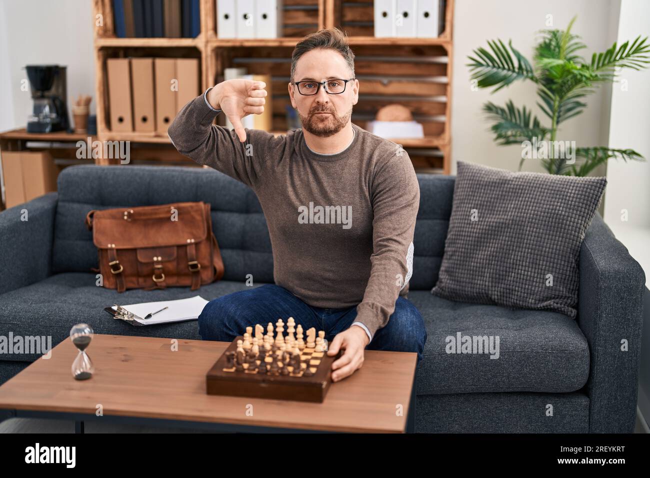 Middle age caucasian man playing chess sitting on the sofa with angry ...