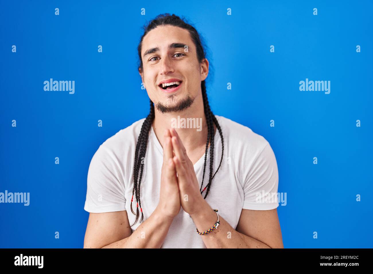 Hispanic man with long hair standing over blue background begging and ...