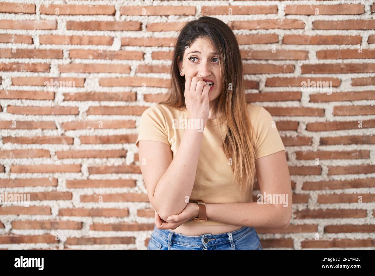 Young brunette woman standing over bricks wall looking stressed and ...