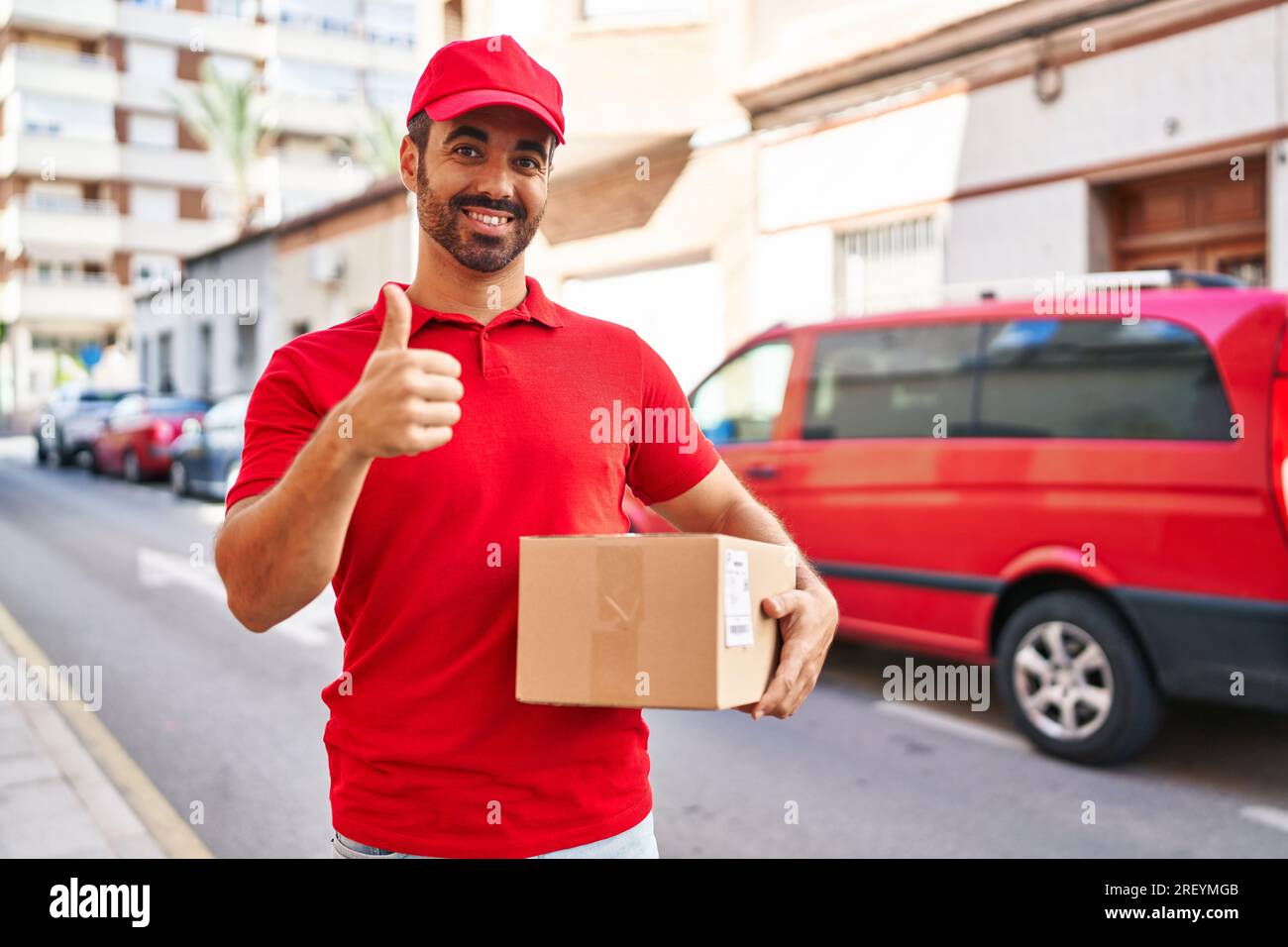 Young hispanic man with beard wearing delivery uniform and cap holding ...