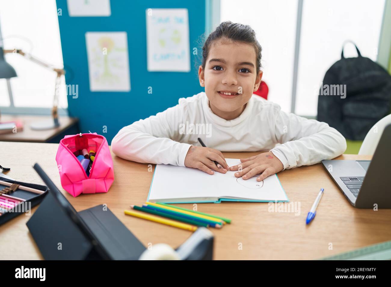 Adorable hispanic girl student writing on notebook at classroom Stock ...