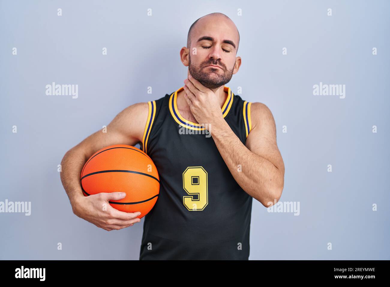 Young bald man with beard wearing basketball uniform holding ball ...