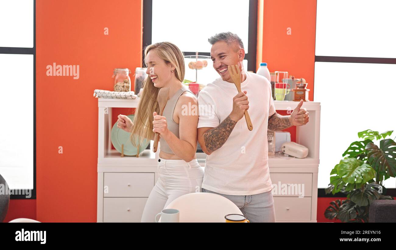 Man and woman couple singing song and dancing using kitchen utensil as ...