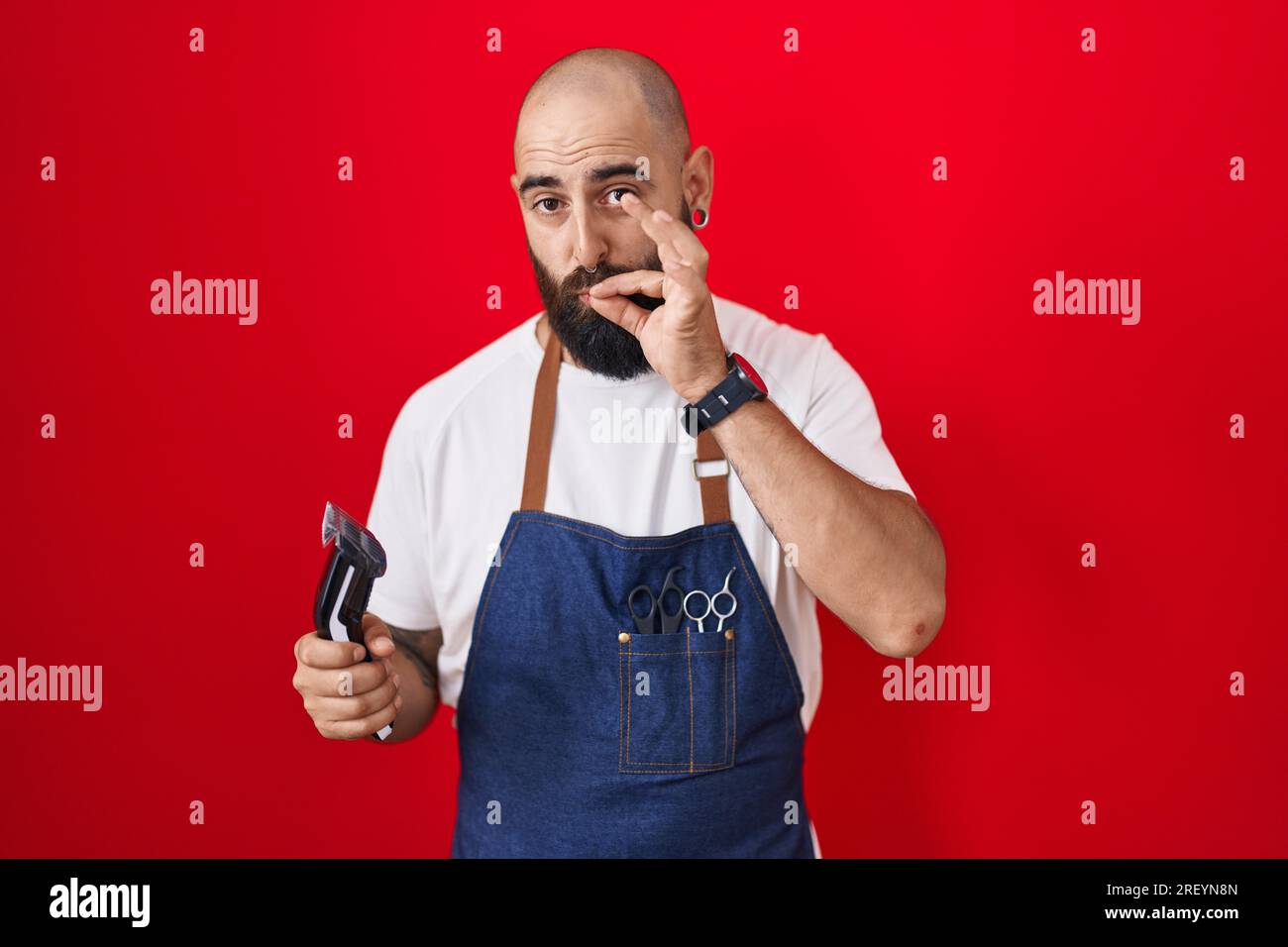 Young hispanic man with beard and tattoos wearing barber apron holding ...