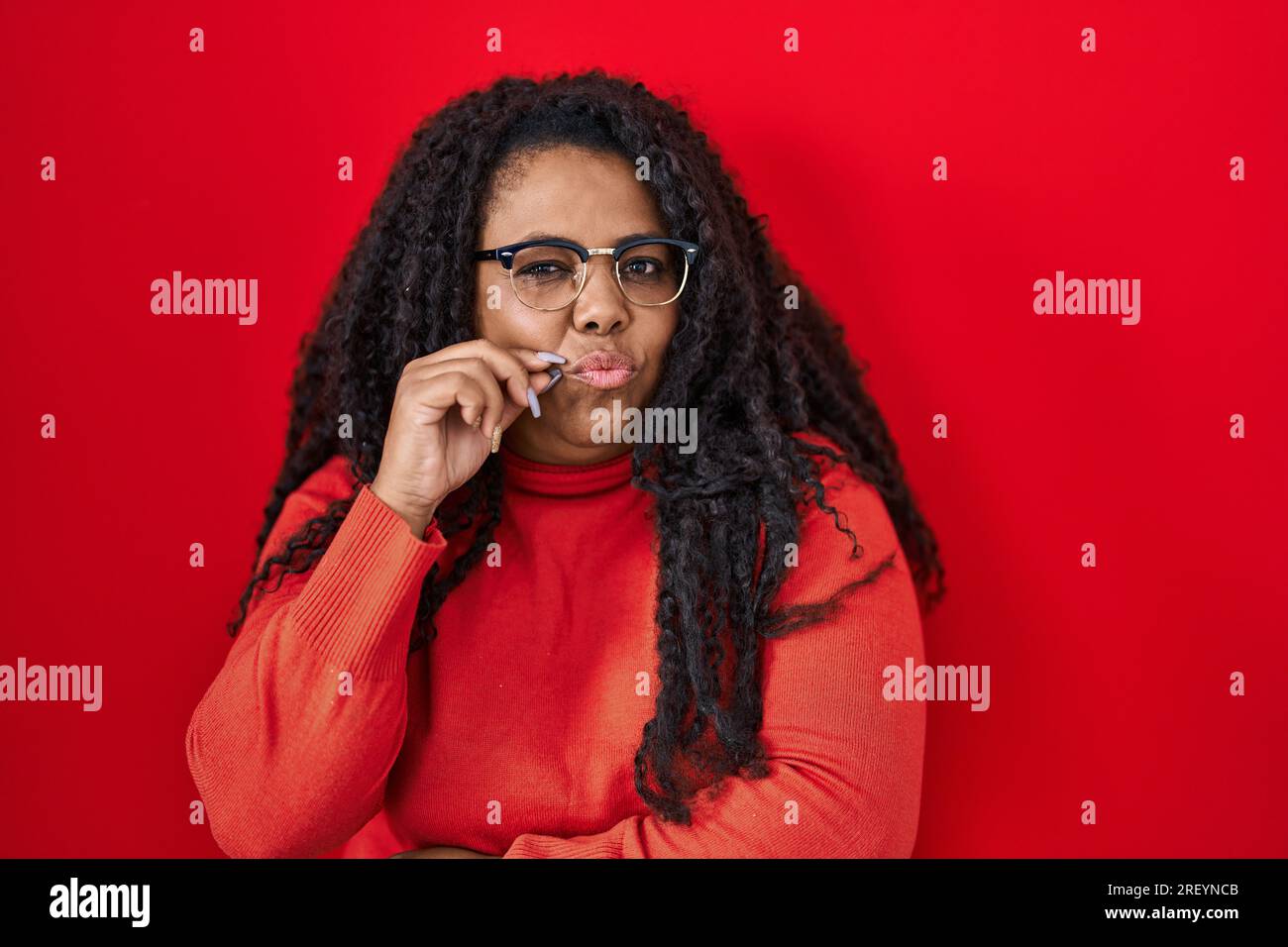 Plus size hispanic woman standing over red background mouth and lips shut as zip with fingers ...