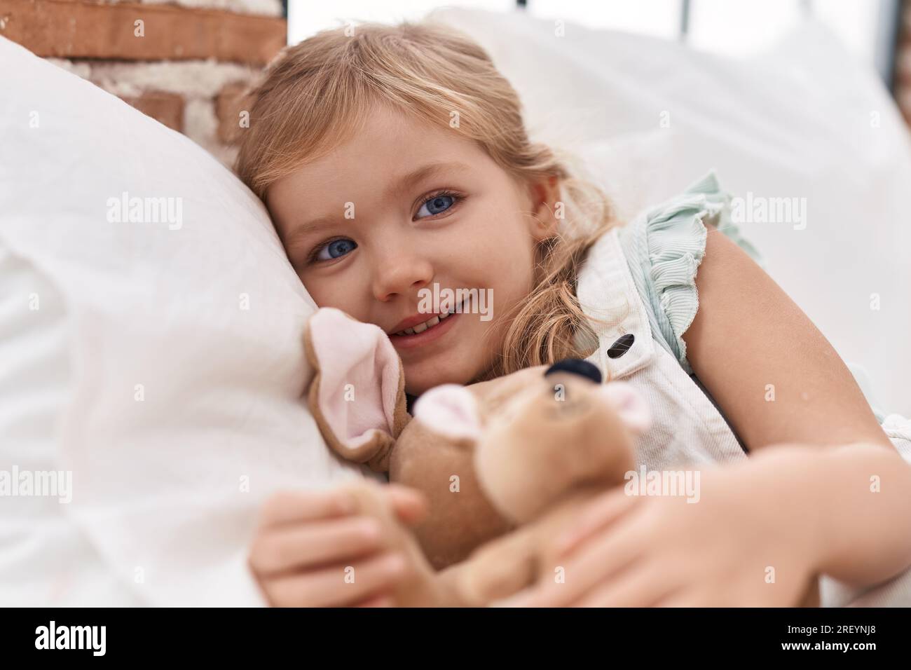Adorable blonde girl holding doll lying on bed at bedroom Stock Photo ...