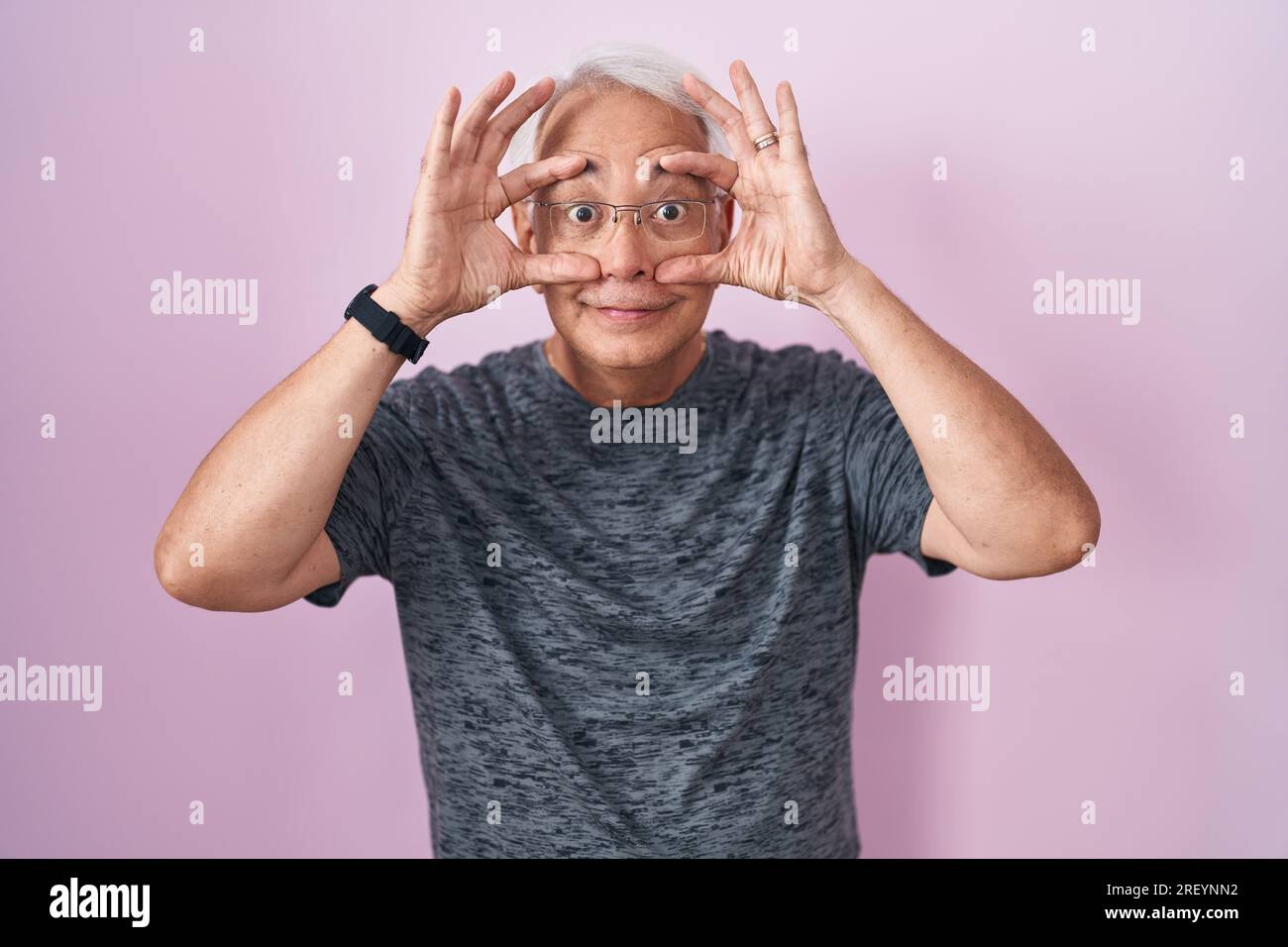 Middle age man with grey hair standing over pink background trying to ...