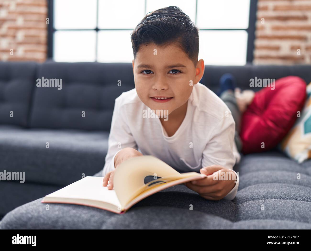 Adorable hispanic boy reading book lying on sofa at home Stock Photo ...