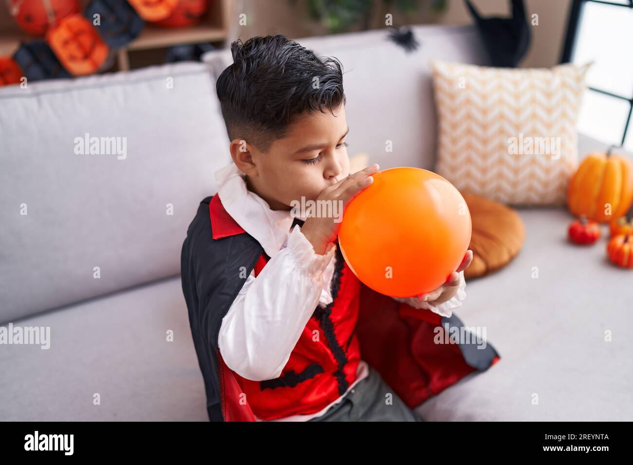 Adorable hispanic boy wearing halloween costume inflating balloon at ...