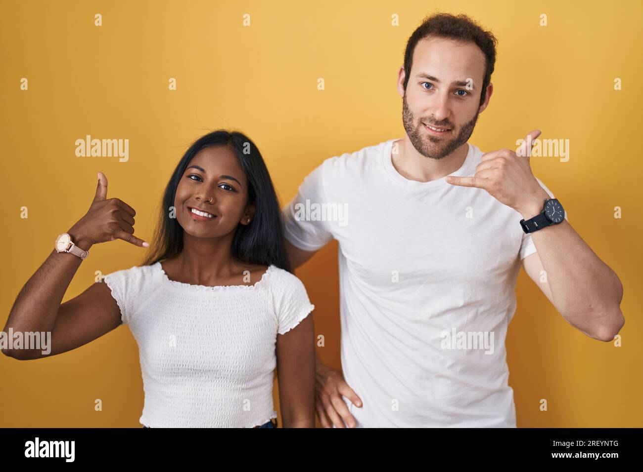Interracial couple standing over yellow background smiling doing phone ...