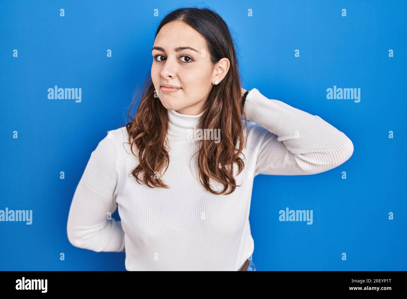 Young hispanic woman standing over blue background suffering of neck ...