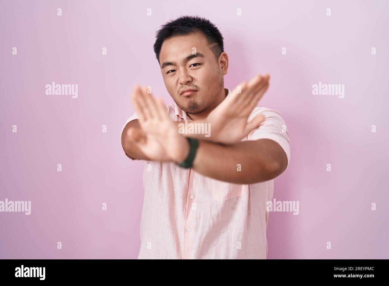 Chinese young man standing over pink background rejection expression ...