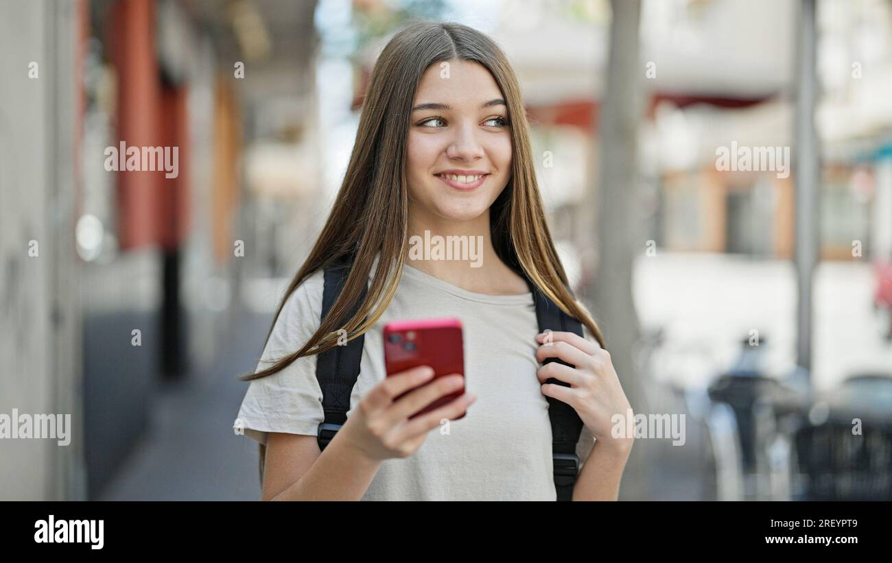 Young beautiful girl student wearing backpack using smartphone at ...