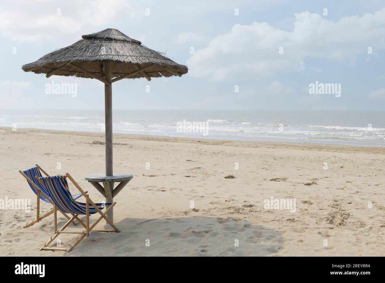 Deserted beach somewhere on the sea. Two beach chairs, a straw umbrella ...