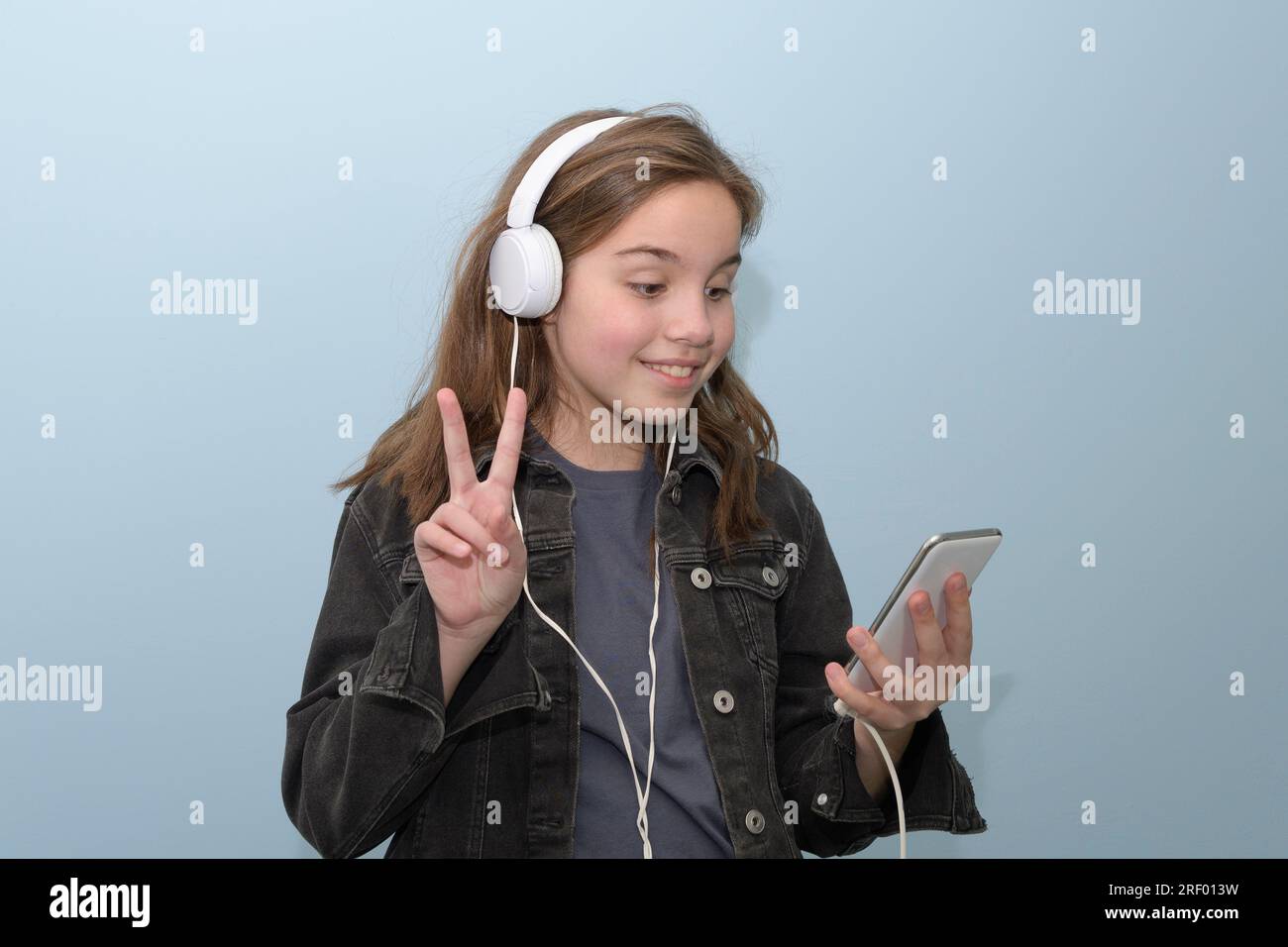 A teenage girl with a white mobile phone and white headphones greets a ...