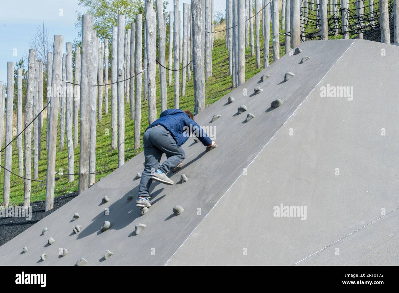Boy climbs a wall in a children's play park in nature. spring time ...